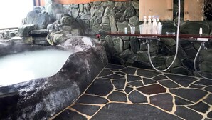 Área de spa com piso de pedra, banheira de hidromassagem, painéis de parede em madeira e chuveiro.