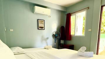 Quarto de hotel com duas camas, um ventilador de teto, uma janela com cortinas vermelhas e um ar condicionado fixado na parede.