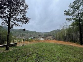 Um campo gramado com lago e árvores ao fundo.