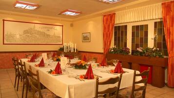 Uma sala de jantar com mesas preparadas para uma refeição, um grande mapa histórico emoldurado na parede e uma janela com cortinas.