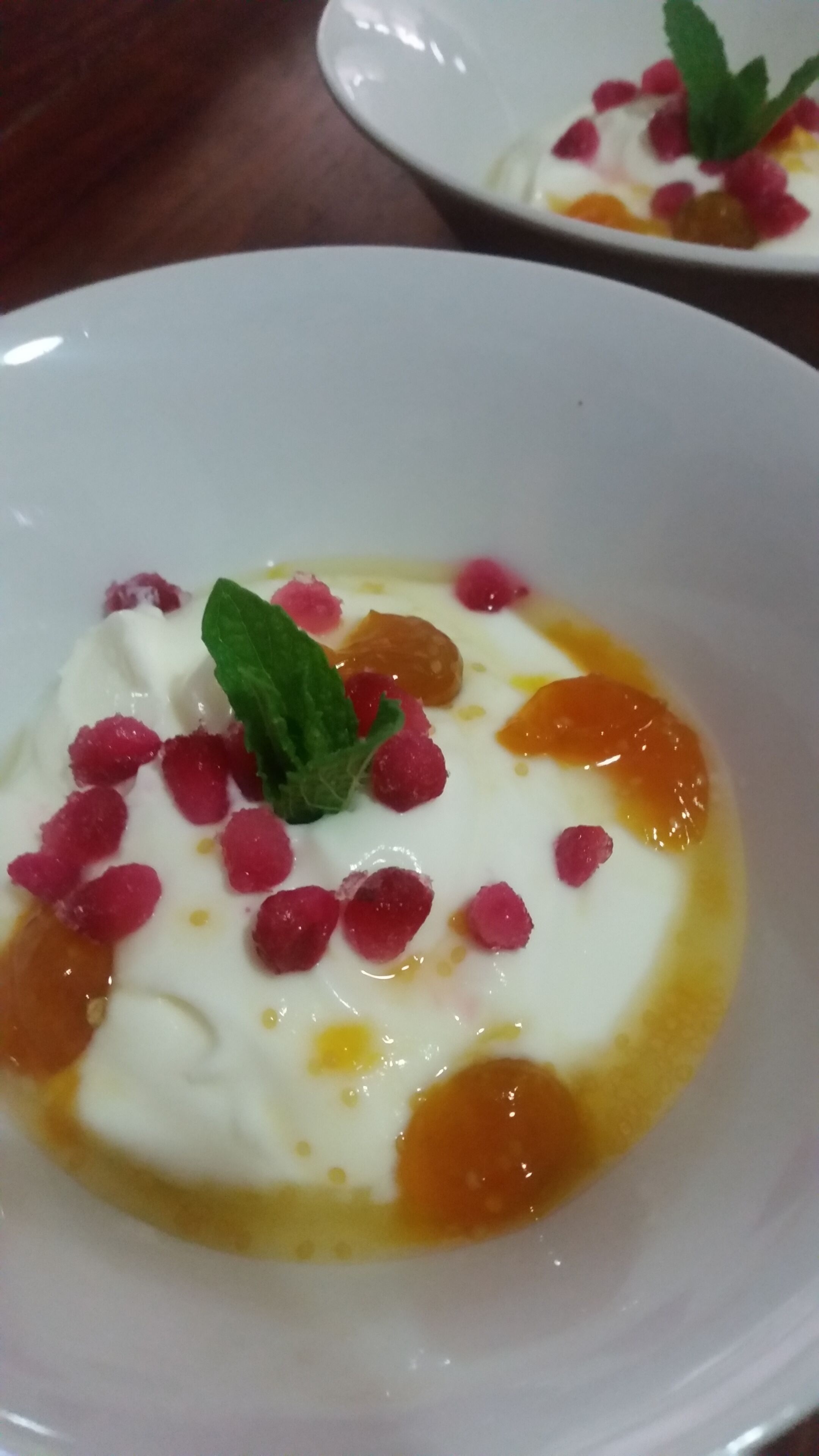 Sobremesa com iogurte, framboesas e gomos de laranja num prato branco.