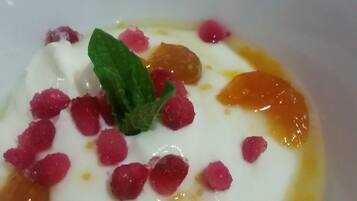 Sobremesa com iogurte, framboesas e gomos de laranja num prato branco.