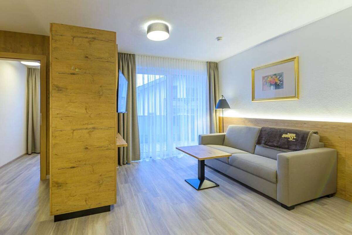 Quarto de hotel moderno com divisória de madeira, sofá, mesinha e abajur.