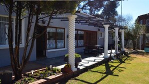 Uma casa com varanda coberta, jardim com plantas e cerca de madeira.
