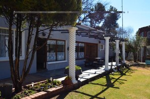 Uma casa com varanda coberta, jardim com plantas e cerca de madeira.