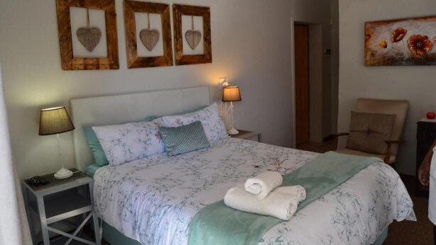 Uma cama bem arrumada com roupa de cama florida, duas luminárias de cabeceira e arte de parede em formato de coração.