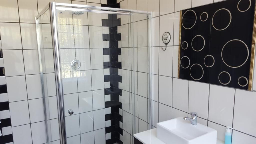 Casa de banho com cabine de chuveiro em vidro, lavatório branco e parede com mosaico preto e branco.
