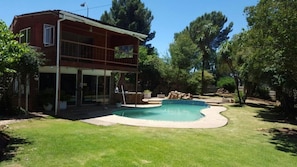 Uma casa de dois andares com piscina, cercada por árvores e um gramado bem cuidado.