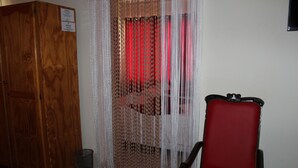 Quarto com guarda-roupa de madeira, uma cadeira vermelha e cortina estampada em vermelho.
