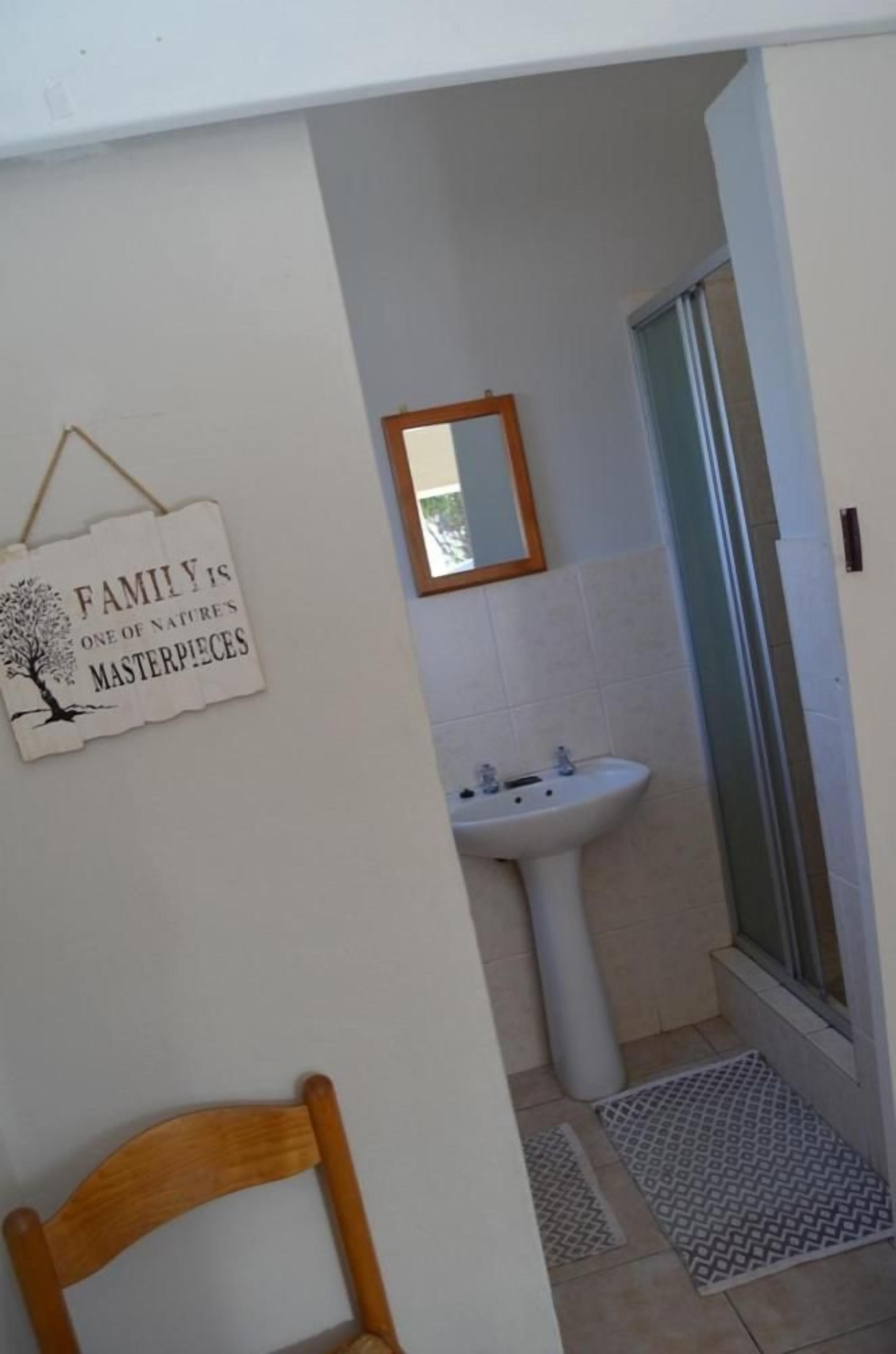 Casa de banho com lavatório branco, espelho e chuveiro. Um aviso na parede diz: 'Família é uma das obras-primas da natureza'.