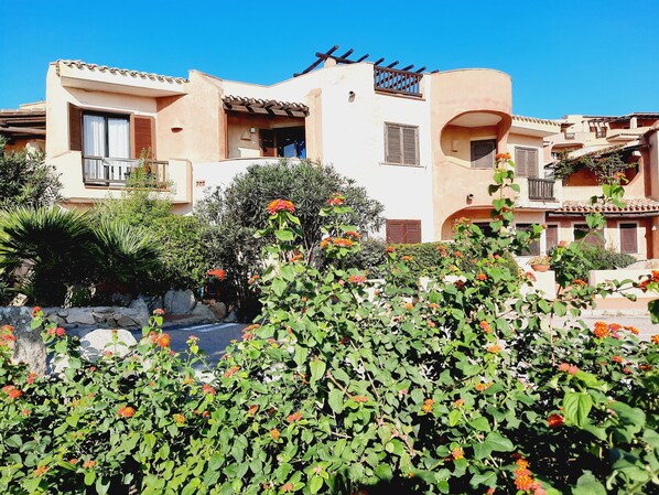Um edifício em estilo mediterrâneo, com fachada em estuque, telhas de barro e uma varanda com guarda-corpo de madeira.