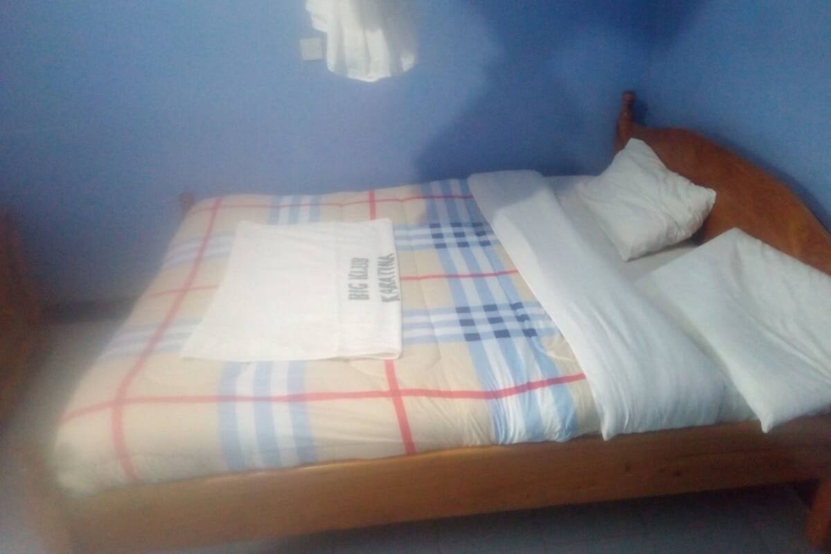 Uma cama de solteiro com um espreador xadrez, um travesseiro branco e uma toalha branca dobrada.