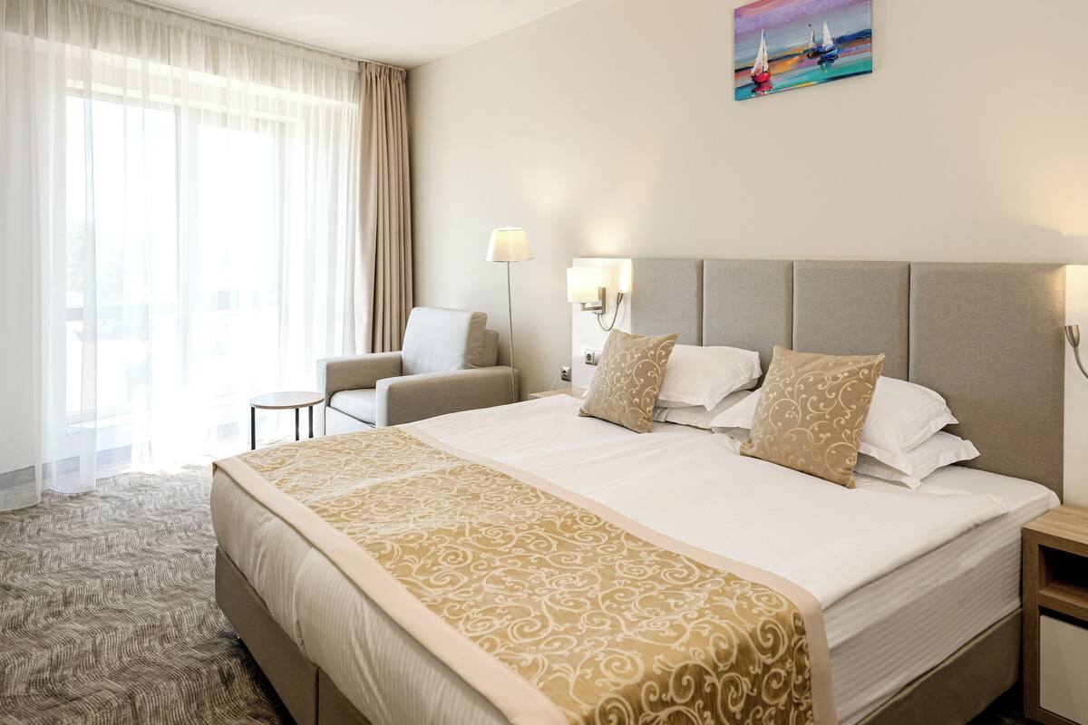 Quarto de hotel com uma cama grande, uma cadeira, uma mesinha e um quadro na parede.