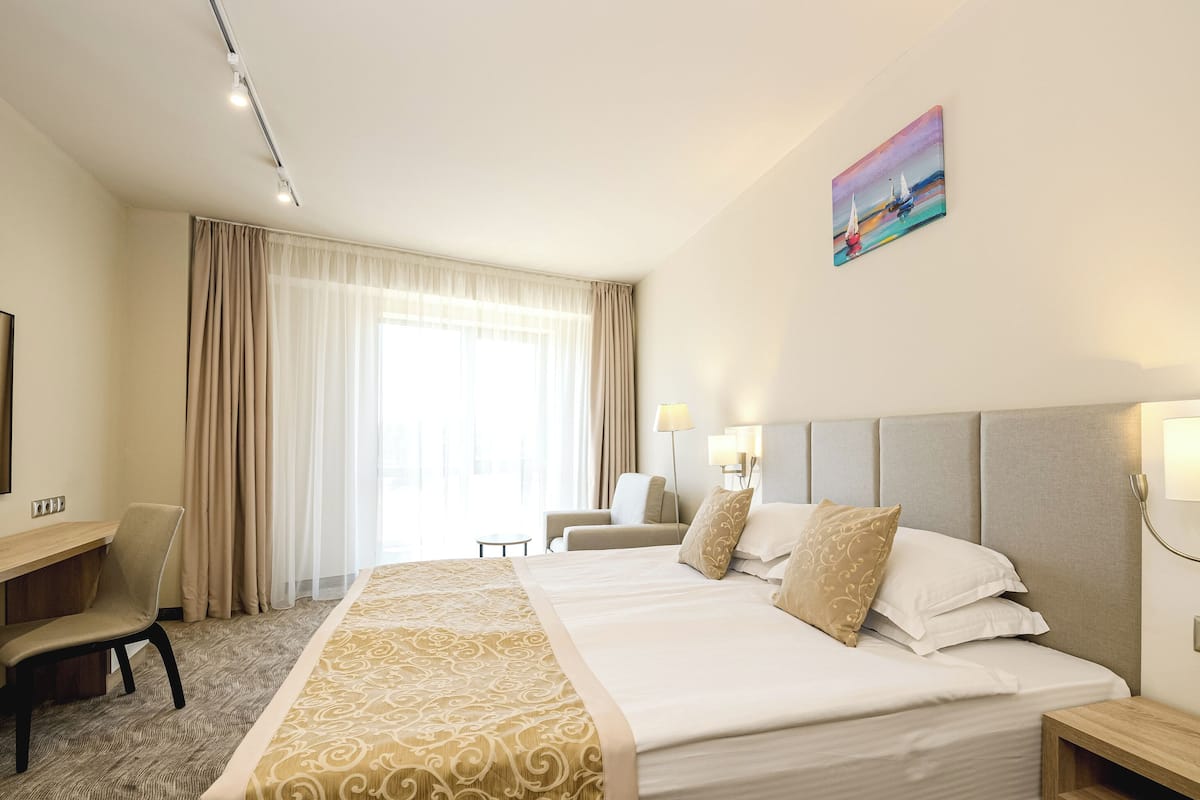 Quarto de hotel com uma cama grande, uma escrivaninha, uma cadeira e um quadro na parede.
