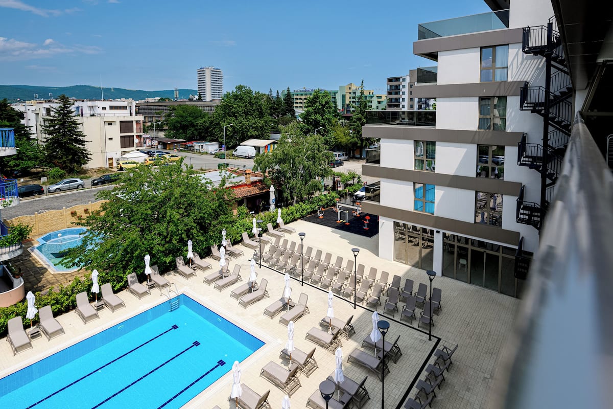 Área de piscina no terraço, com espreguiçadeiras e guarda-sóis, cercada por edifícios e árvores.