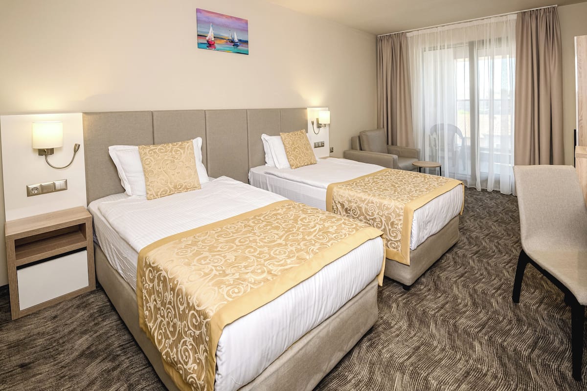 Quarto de hotel com duas camas, um sofá, uma mesinha e uma janela com cortinas.