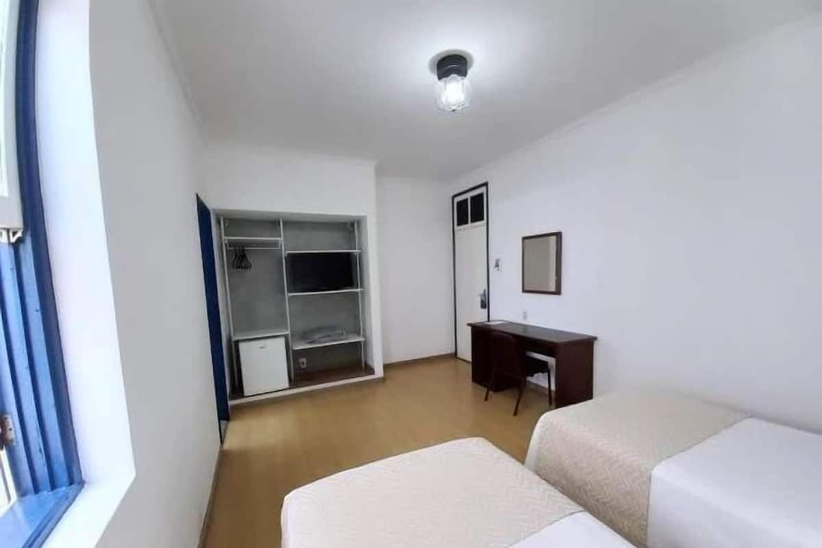 Quarto com cama, escrivaninha, guarda-roupa e janela.