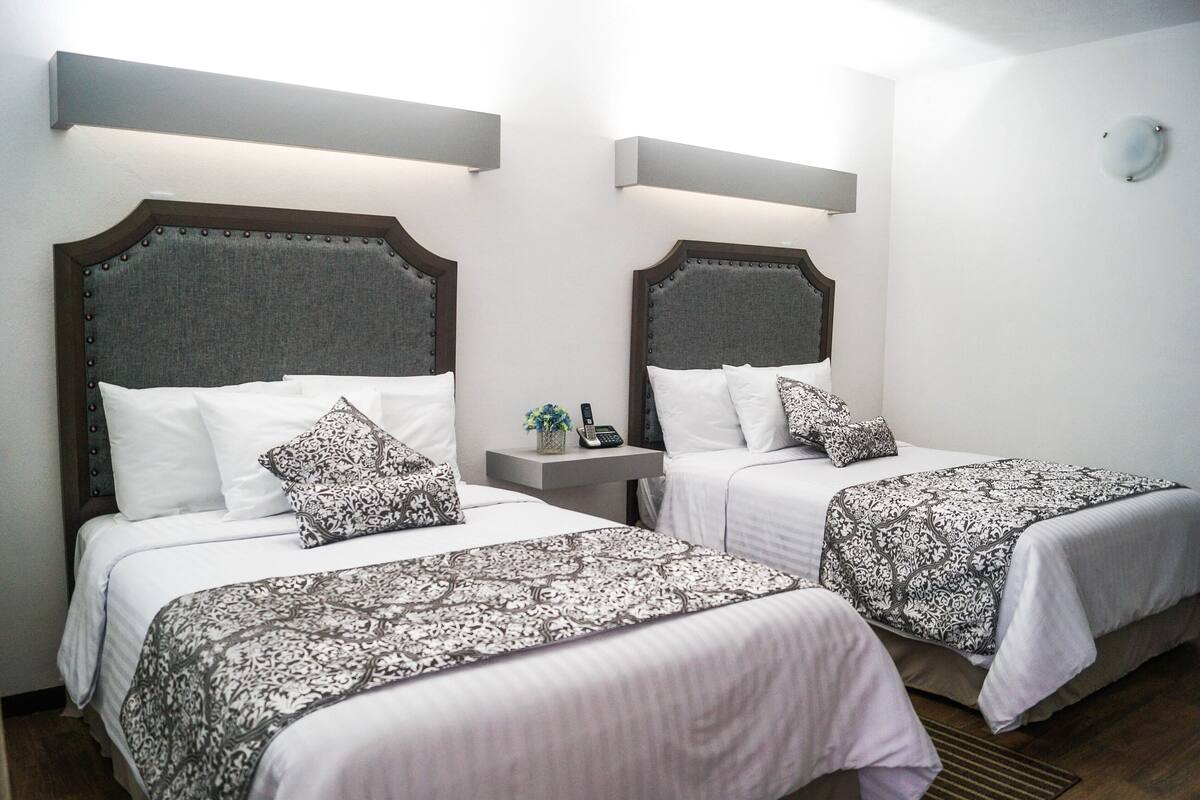 Duas camas de solteiro com cabeceiras, roupa de cama branca e mantas decoradas.
