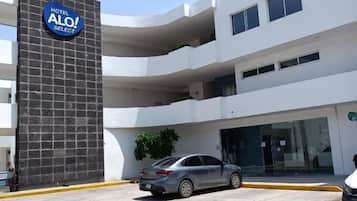 Um hotel com uma placa visível, estacionamento e fachada de edifício moderna.