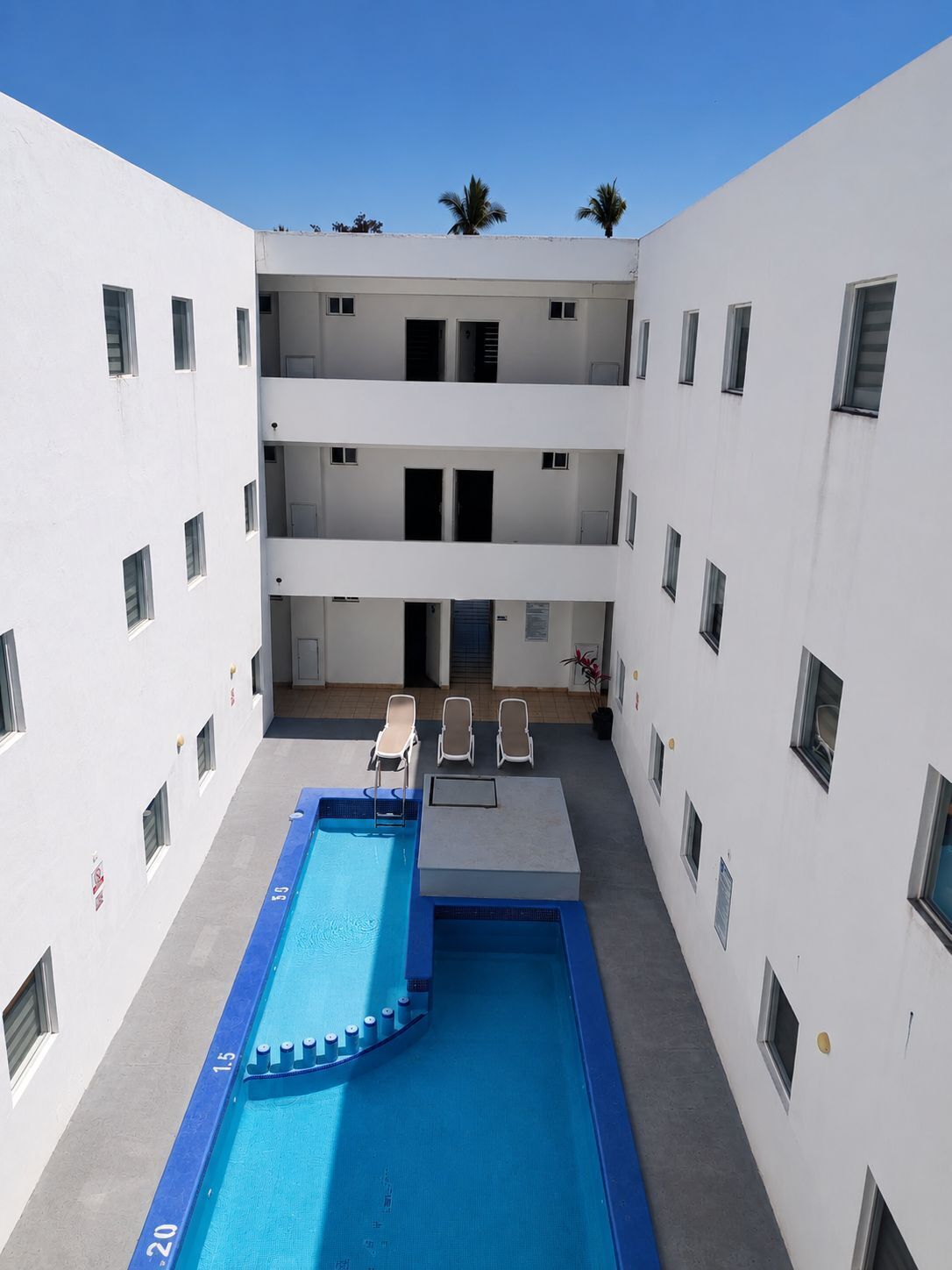 Edifício de vários andares com um pátio central, piscina e espreguiçadeiras.