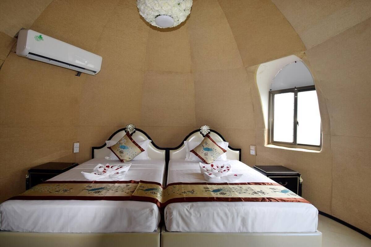 Quarto com duas camas, ar condicionado, uma pequena janela e uma luminária decorativa no teto.