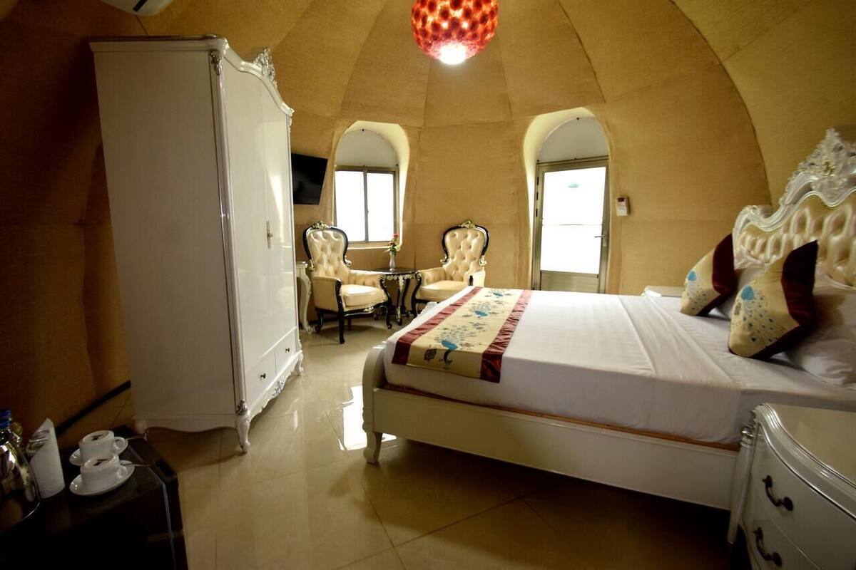 Quarto com uma cama grande, guarda-roupa, duas poltronas, uma mesinha e um candelabro.