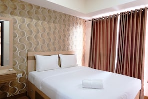Quarto de hotel com papel de parede estampado, cabeceira de madeira, cama branca com duas almofadas, toalha dobrada e janela com cortinas.
