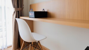 Quarto de hotel com prateleira de madeira, uma cadeira branca e um minibar.