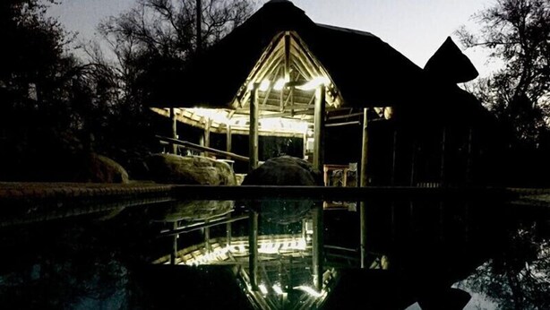 Um edifício com fachada de vidro refletindo na água, rodeado por árvores.