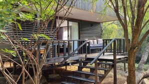 Uma cabana com varanda, sofá e escada que leva à entrada.