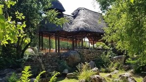 Uma construção com telhado de palha e um pavilhão de madeira, rodeada por pedras e vegetação.