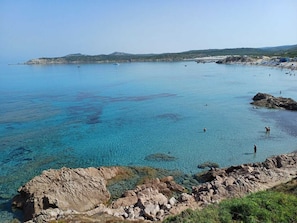 Uma área costeira com águas azul-claras, linhas de costa rochosas e colinas ao longe.