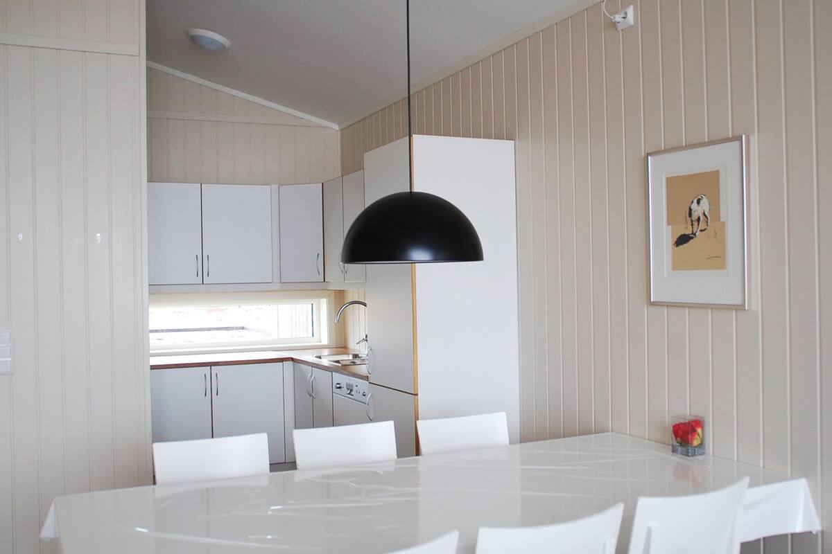 Uma cozinha moderna com armários brancos, uma luminária pendente preta e uma mesa de jantar com cadeiras.