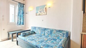 Um quarto com um sofá de padrão azul, uma mesa pequena, uma janela com cortinas e um luminário fixado na parede.