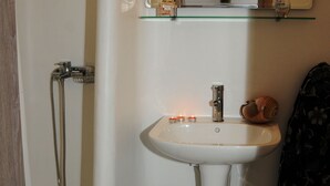 Casa de banho com lavatório branco, espelho, chuveiro e barra de toalhas.