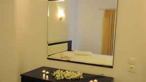 Um quarto com uma cama, uma cômoda e um espelho. Há velas sobre a cômoda.