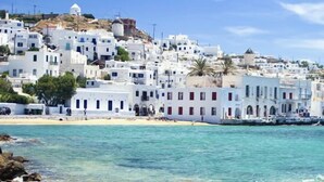 Uma vila costeira com edifícios brancos, uma praia e águas azul-claras.