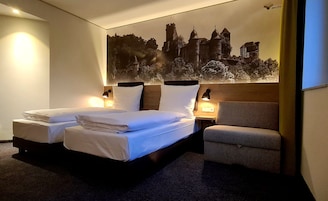 Quarto de hotel com duas camas, uma cadeira e um grande mural na parede retratando um castelo.