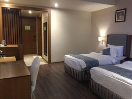 Quarto de hotel com duas camas, uma mesa e uma cadeira.
