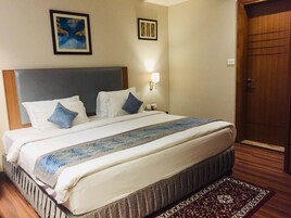 Uma cama bem arrumada com colcha estampada, cabeceira e duas luminárias fixadas na parede.