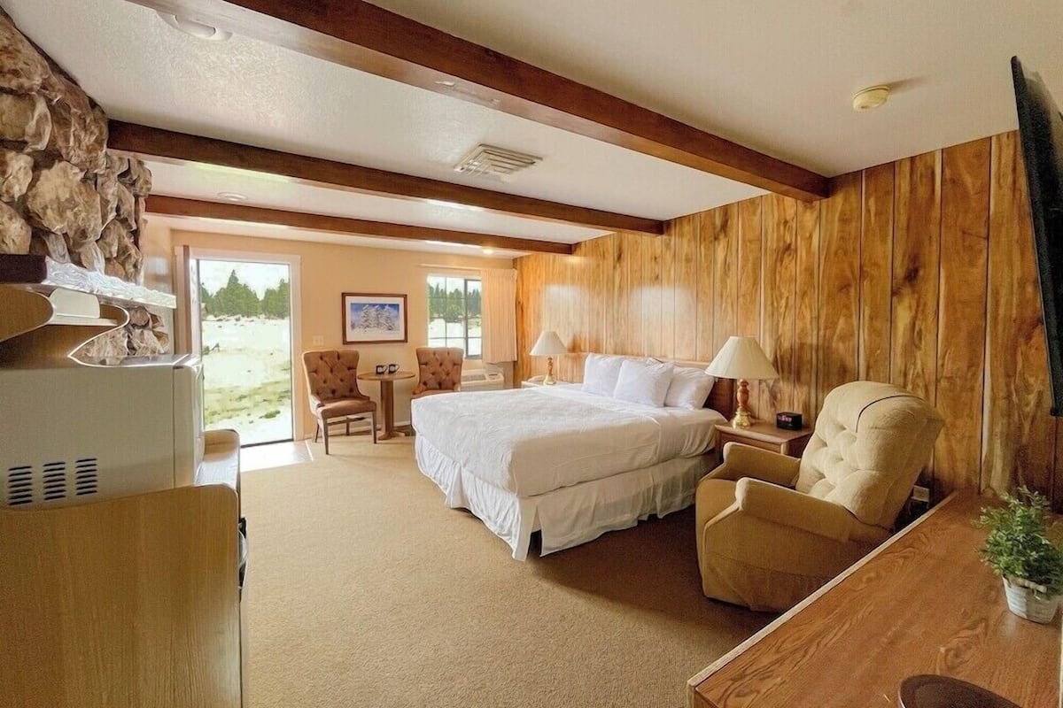 Quarto com cama grande, duas cadeiras, escrivaninha e parede de pedra.