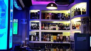 Um bar com várias prateleiras de garrafas de bebidas, um letreiro de neon e uma luminária pendente.