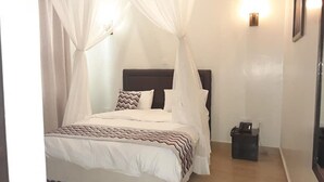 Uma cama bem arrumada com dossel, mesa de cabeceira e luminária fixada na parede.