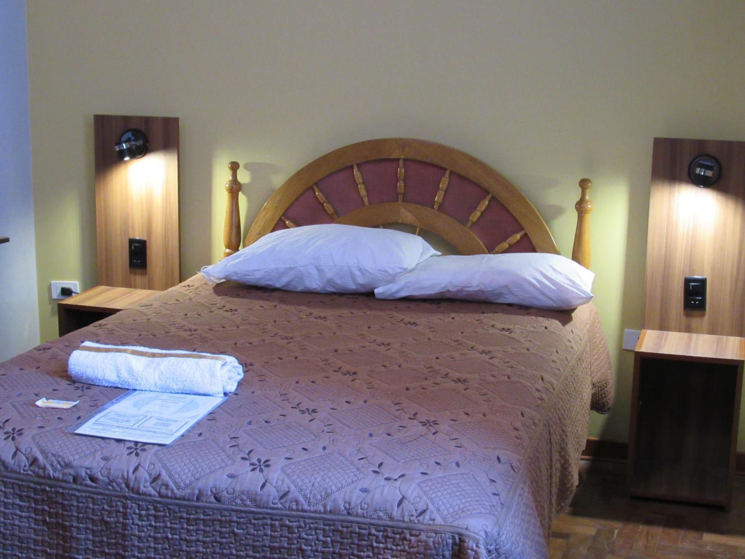 Uma cama bem arrumada com colcha estampada, duas mesas de cabeceira com abajures e uma cabeceira de madeira.