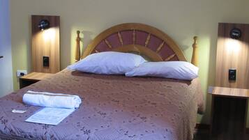 Uma cama bem arrumada com colcha estampada, duas mesas de cabeceira com abajures e uma cabeceira de madeira.