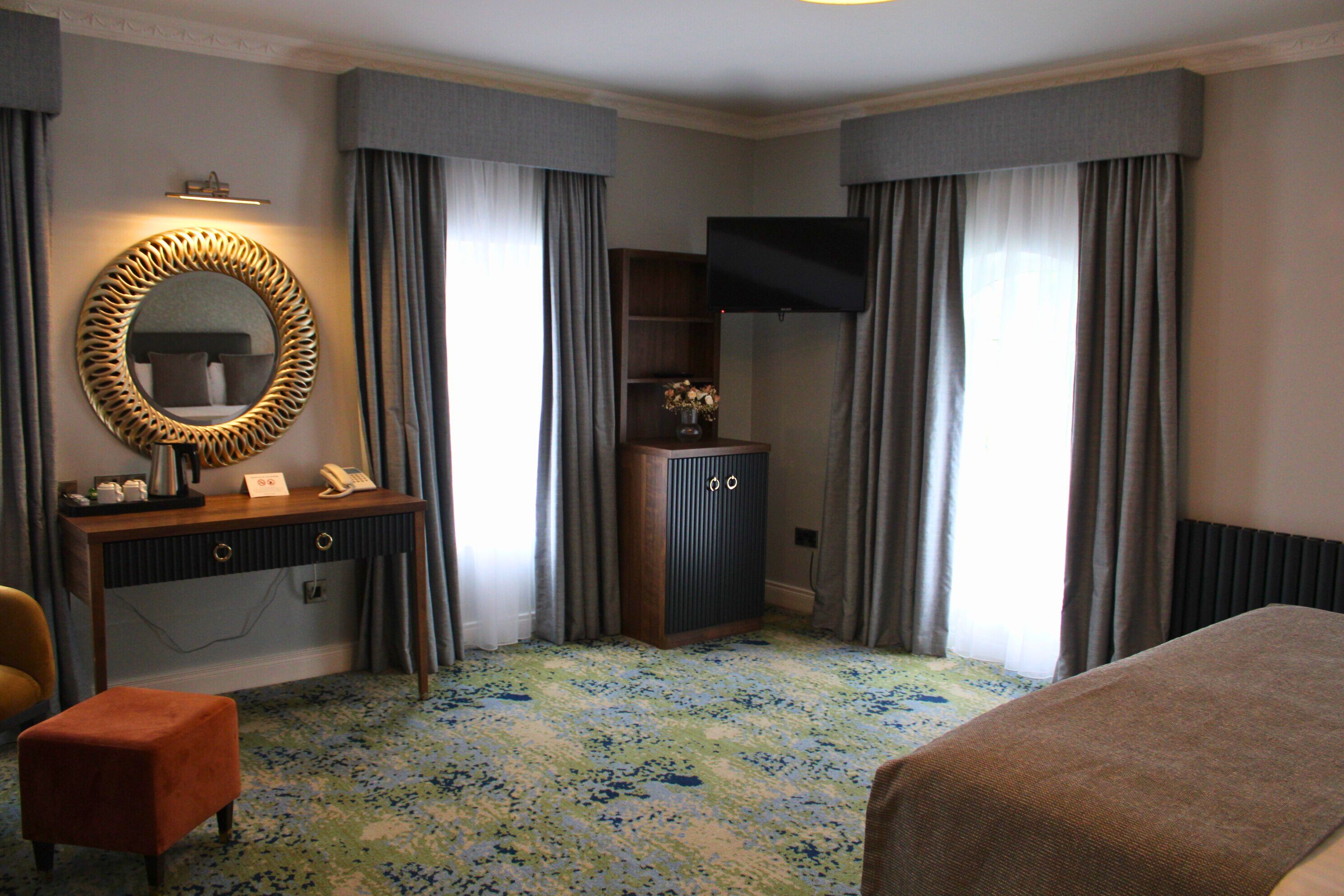 Quarto de hotel com cama, secretária com telefone, espelho, televisão e armário.