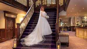 Uma escadaria imponente com grades ornamentadas, um balcão de recepção e um candelabro.