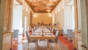Uma longa mesa de jantar com cadeiras, um lustre e um chão estampado.