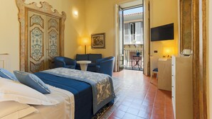 Quarto com cama, duas cadeiras, uma mesinha, televisão e varanda com guarda-corpo.