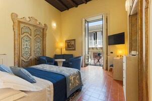 Quarto com cama, duas cadeiras, uma mesinha, televisão e varanda com guarda-corpo.
